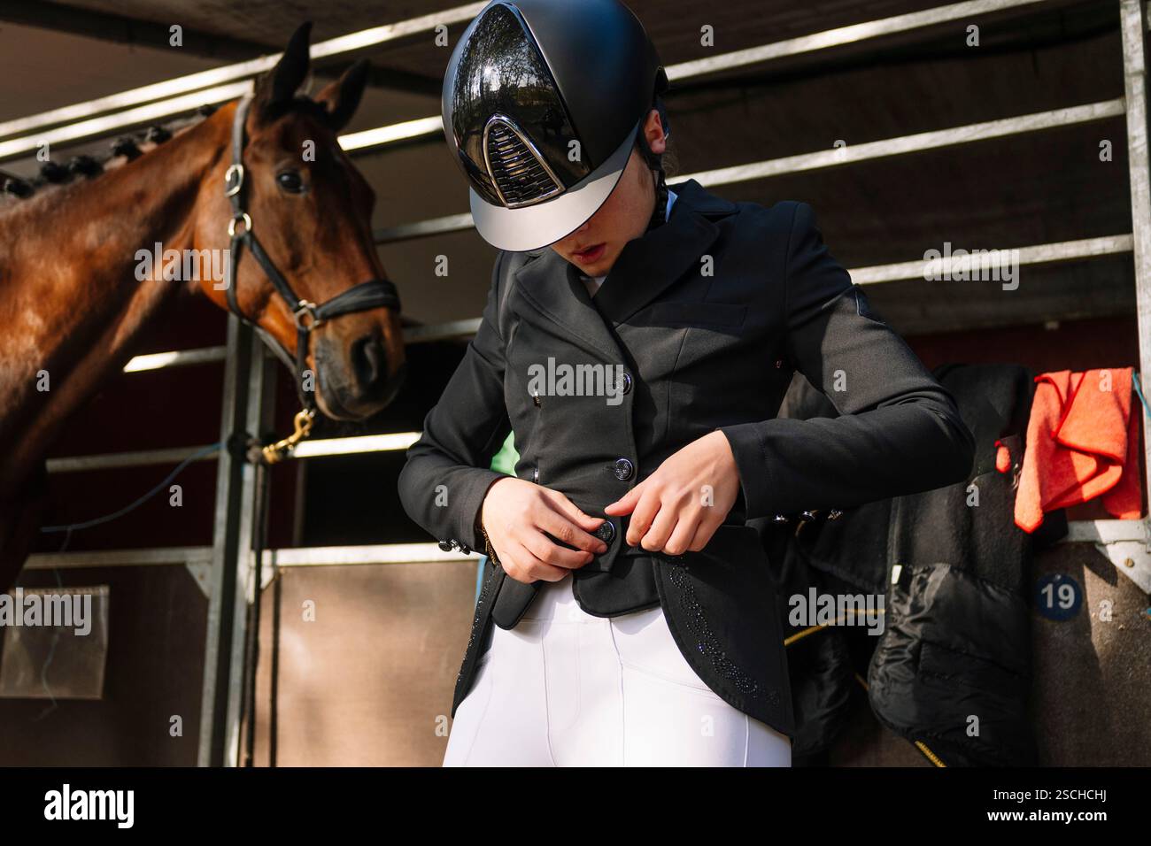 A rider adjusts their outfit in a stable, preparing for a classical ...
