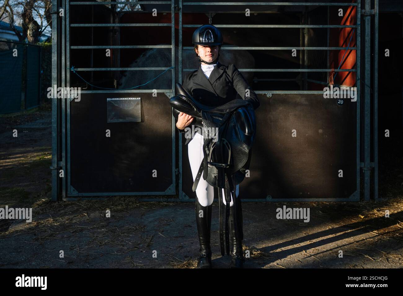 Equestrian preparing for a dressage event, holding a saddle outside a ...
