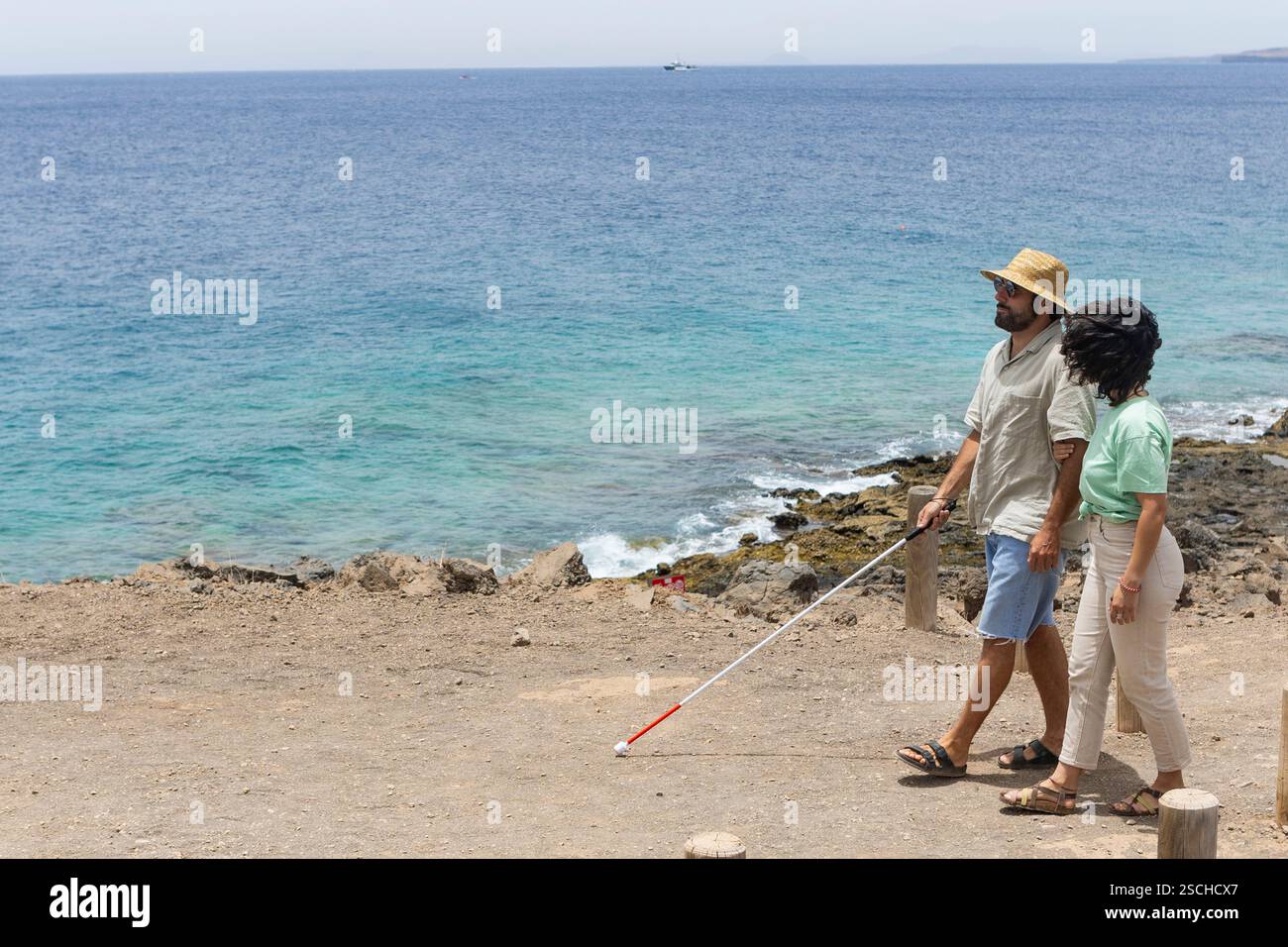 A blind man walks along a coastal path with a female guide, using a ...