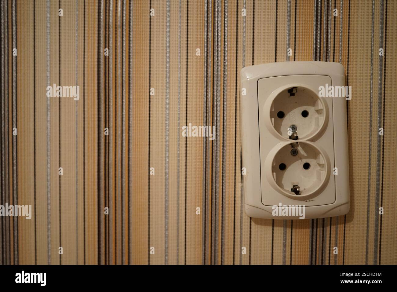 An electric outlet is installed on a wall covered in striped wallpaper ...