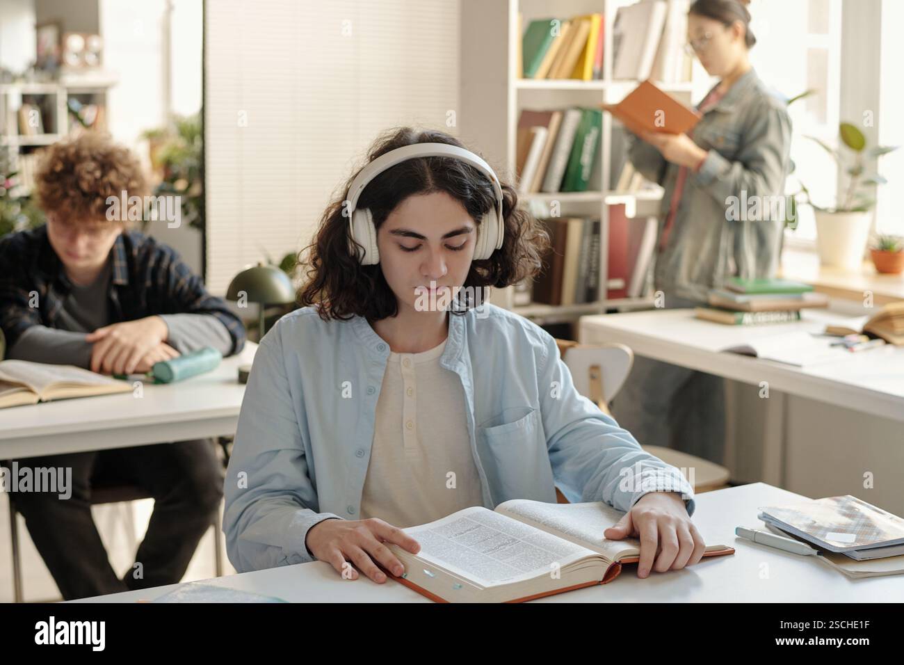 Male Student Wearing Headphones Studying at Desk in College Library ...