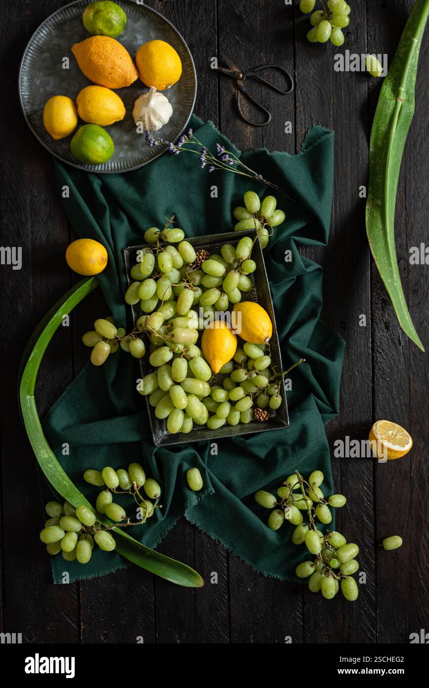 A vibrant display of green grapes, lemons, and limes on a dark wooden ...