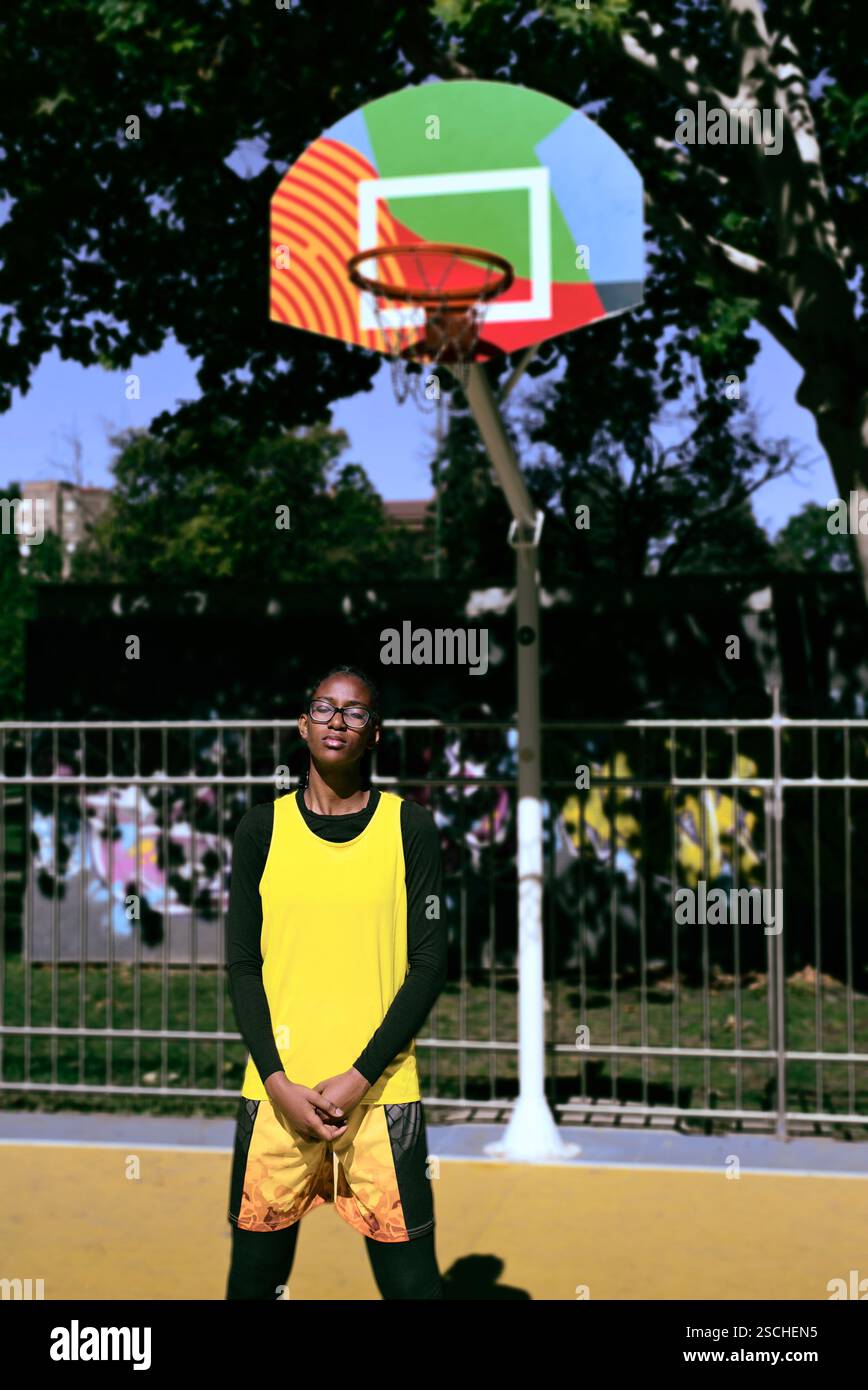 A woman athlete stands confidently on an outdoor basketball court ...