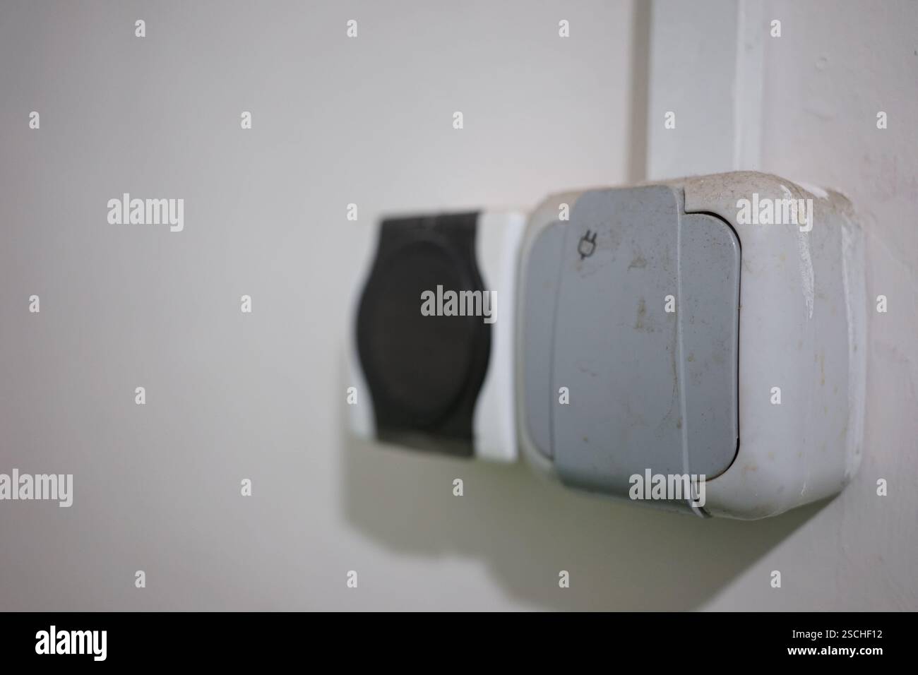 Two power outlets are mounted on a plain white wall. One is round and the other is square ...