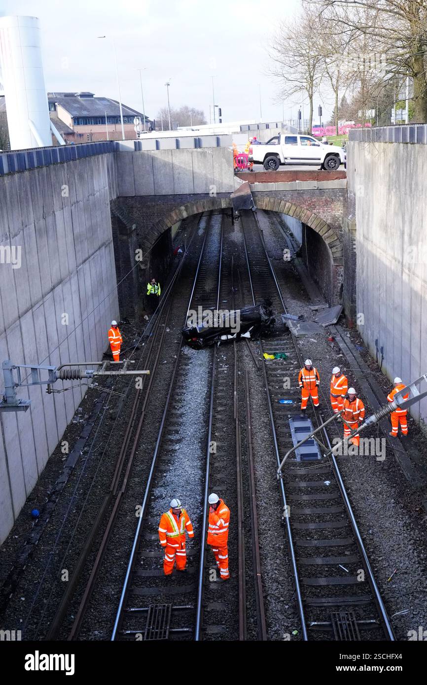 Emergency workers view a car that crashed onto tracks in Salford ...
