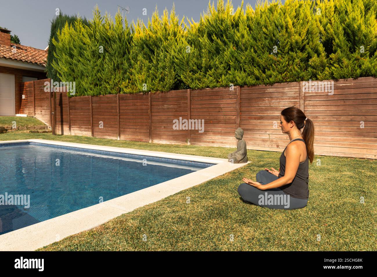 A woman in a yoga Easy Pose (Sukhasana) meditating by a poolside ...