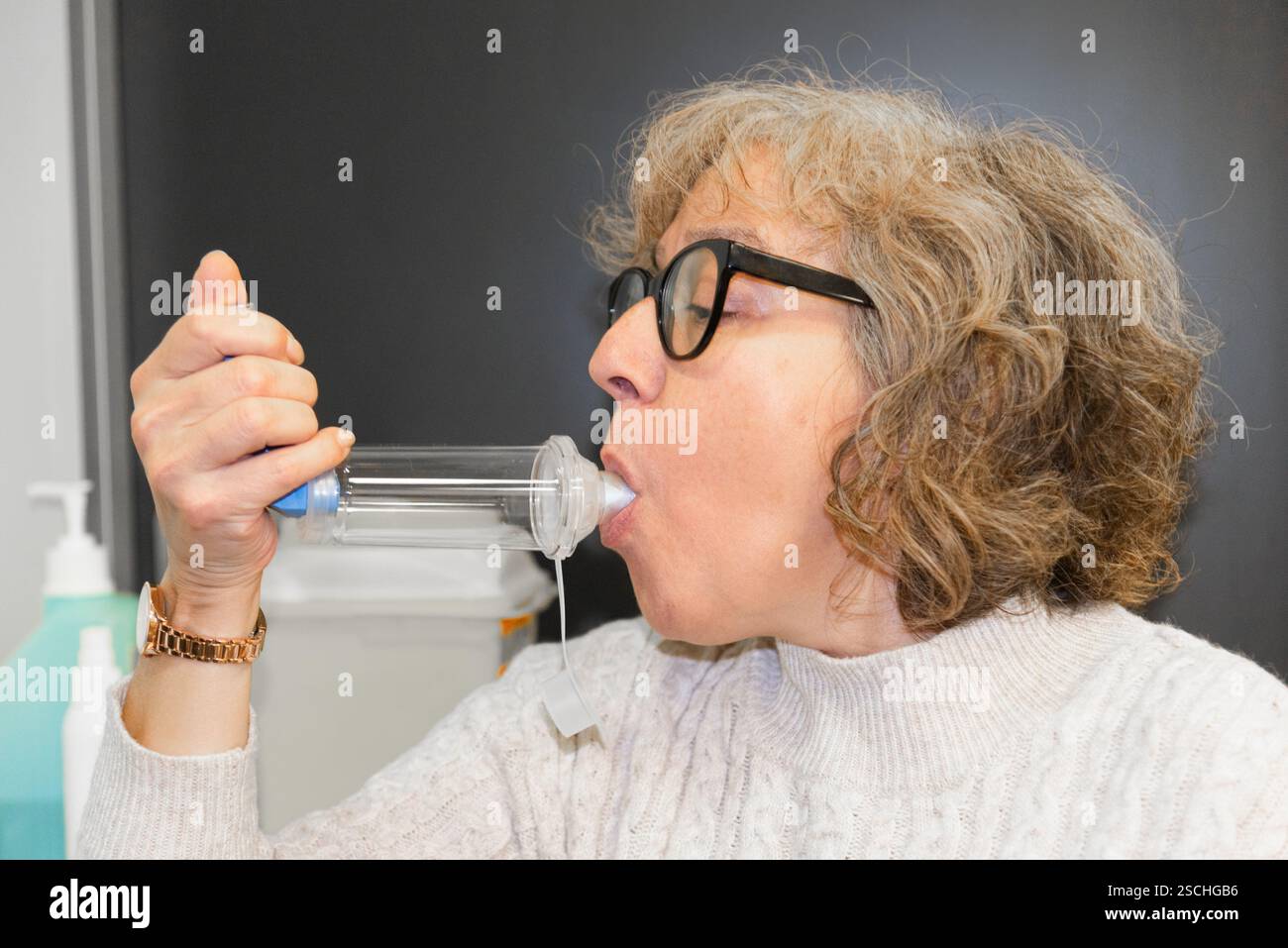 A middle-aged woman with glasses uses a medical inhalation device in a ...