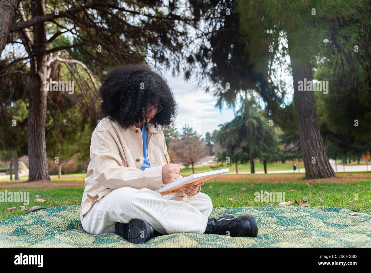 A young black artist sits cross legged on a patterned blanket in a ...