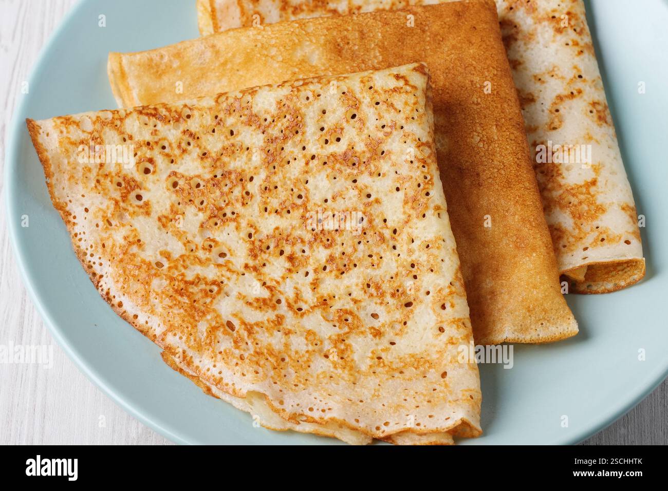 Perfectly cooked golden brown crepes stacked on a light blue plate ...