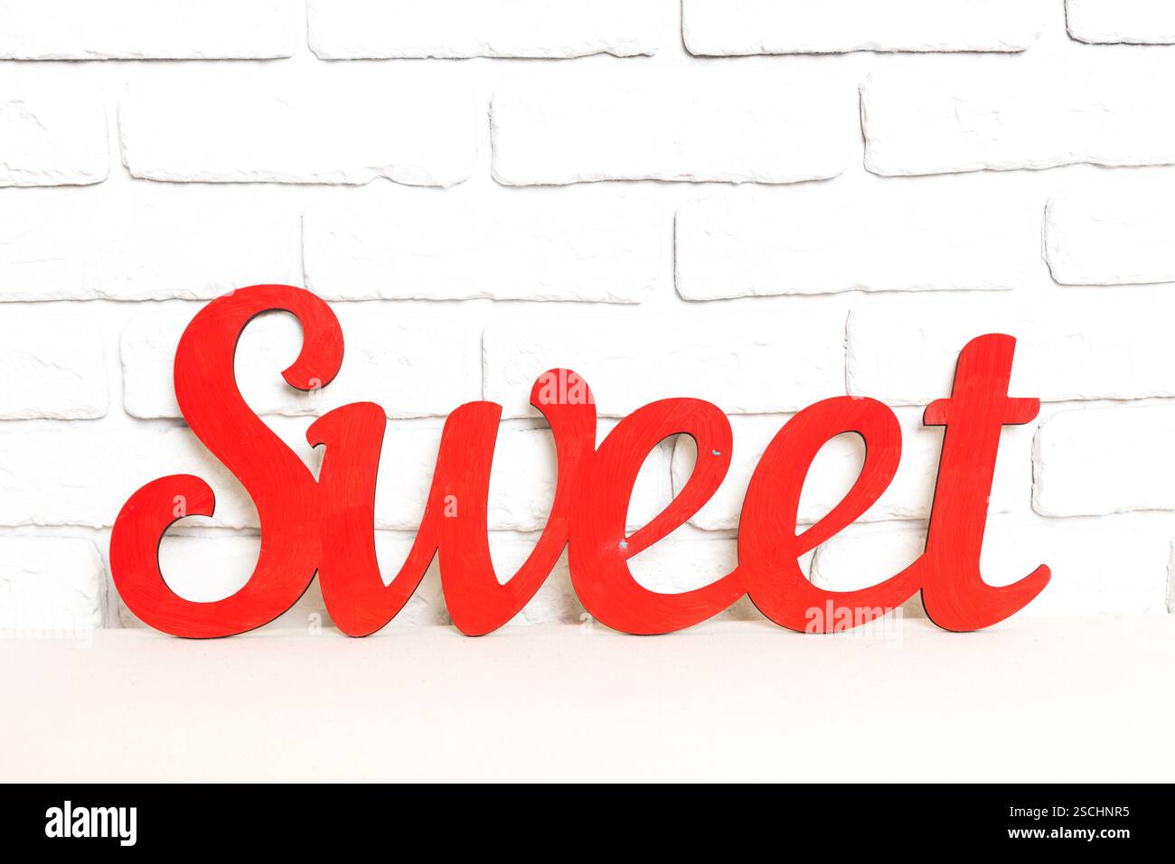 Decorative red sign displaying the word sweet against a white brick ...