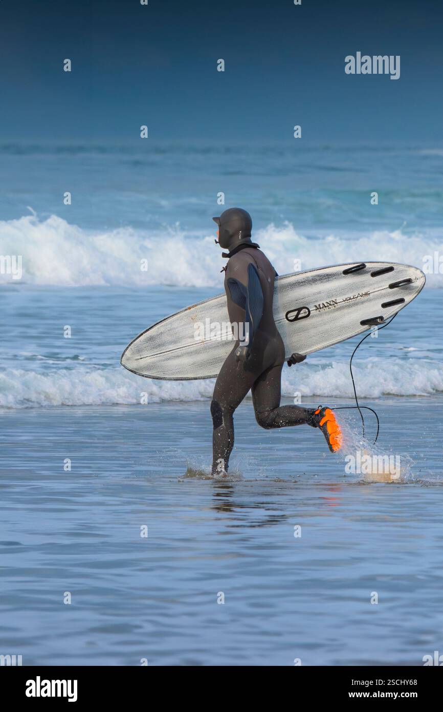 A sufer carrying his surfboard running into the sea at Fistral in ...