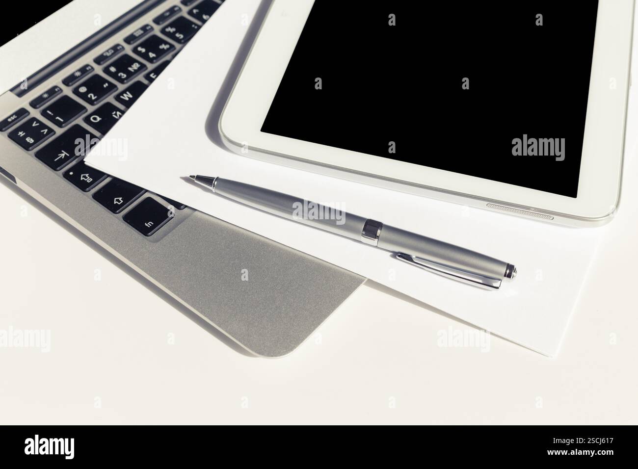 Workspace arrangement with laptop, tablet, pen, and blank paper on desk ...
