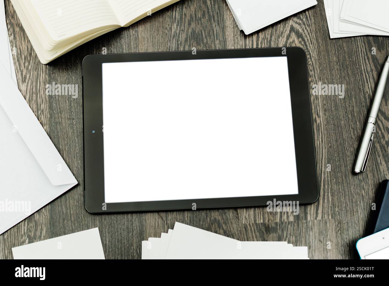 Blank tablet surrounded by writing materials on a wooden desk in a cozy ...