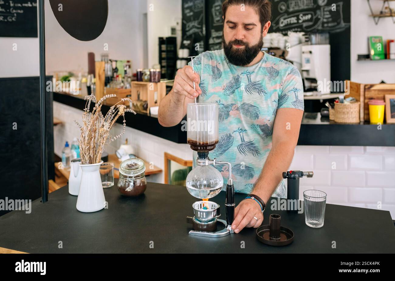 Barista skillfully stirring with spoon a specialty coffee into siphon ...