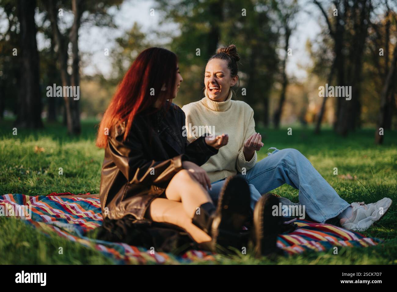 Two friends laughing together while sitting on a picnic blanket ...