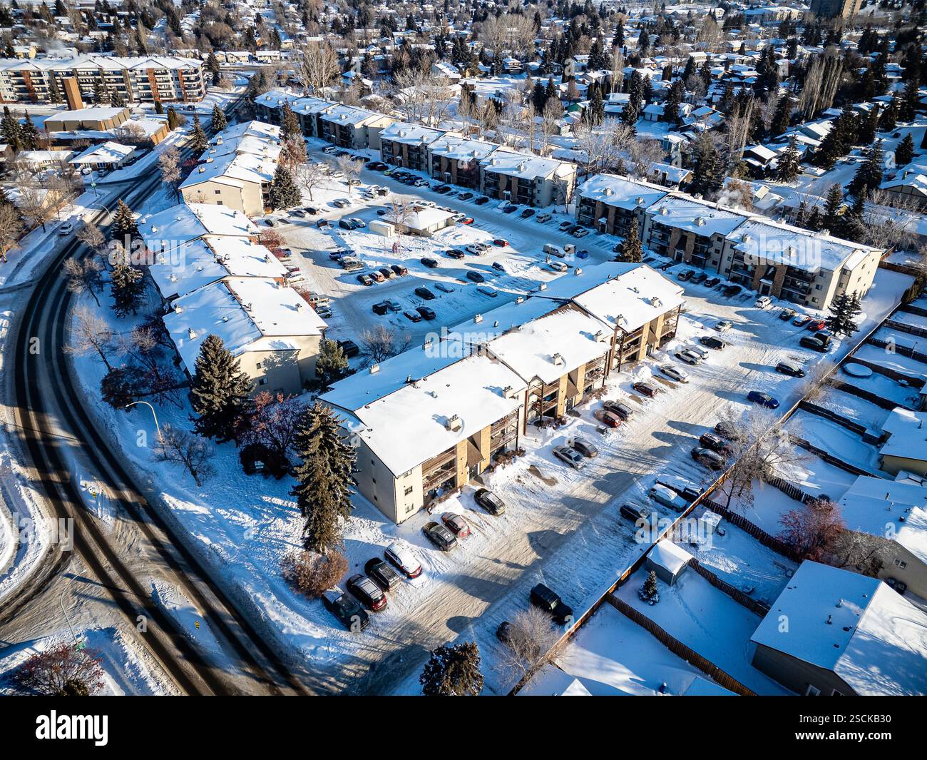 Snowy cityscape with a large apartment complex and a parking lot. The ...