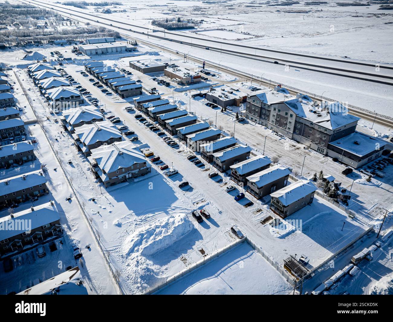 Snowy city street with a row of houses and a few cars. The houses are ...