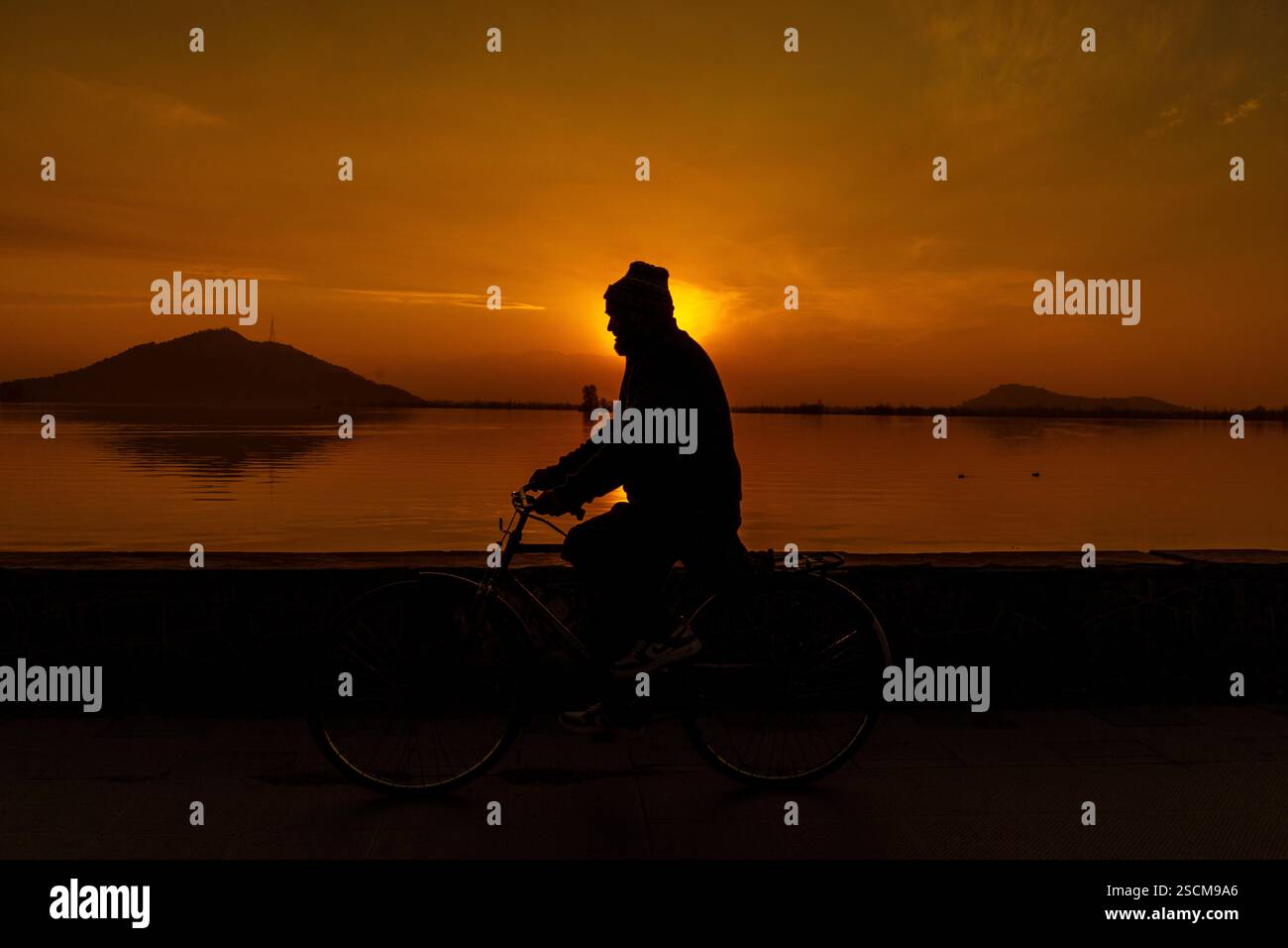 A Kashmiri cyclist rides along the bank of Dal Lake at sunset in ...