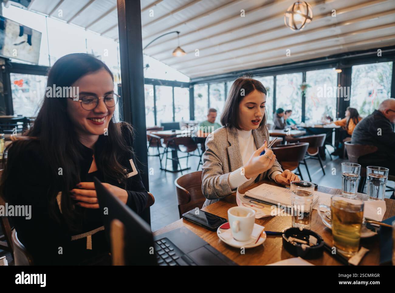 Two women collaborating on business tasks in a modern café setting ...