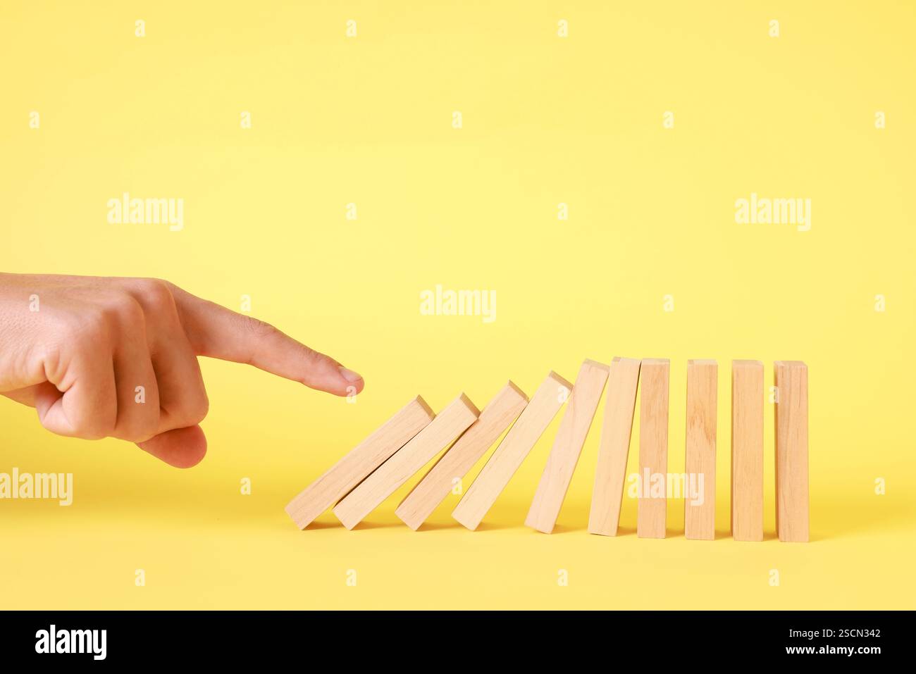 Domino effect. Man pushing wooden blocks on yellow background, closeup ...