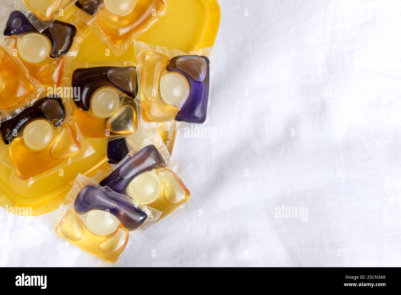 Laundry detergent capsules in container on white fabric, closeup. Space ...