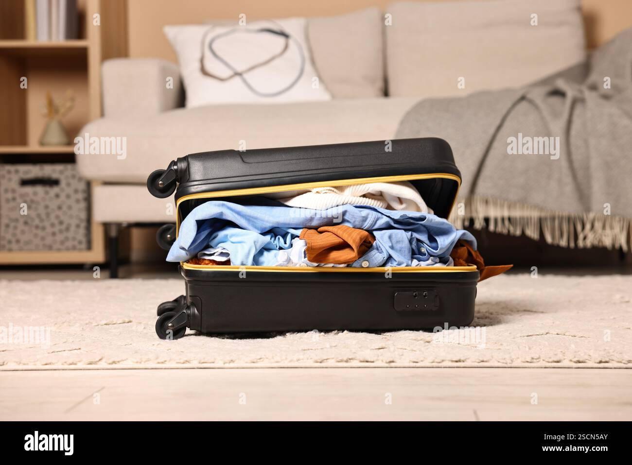 Open suitcase full of different messy clothes on floor indoors Stock ...