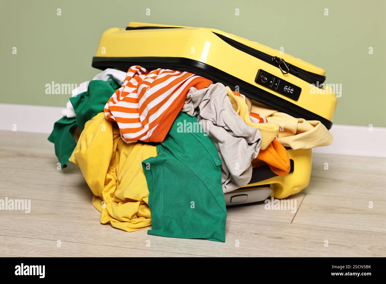 Open suitcase full of different messy clothes on floor indoors Stock ...