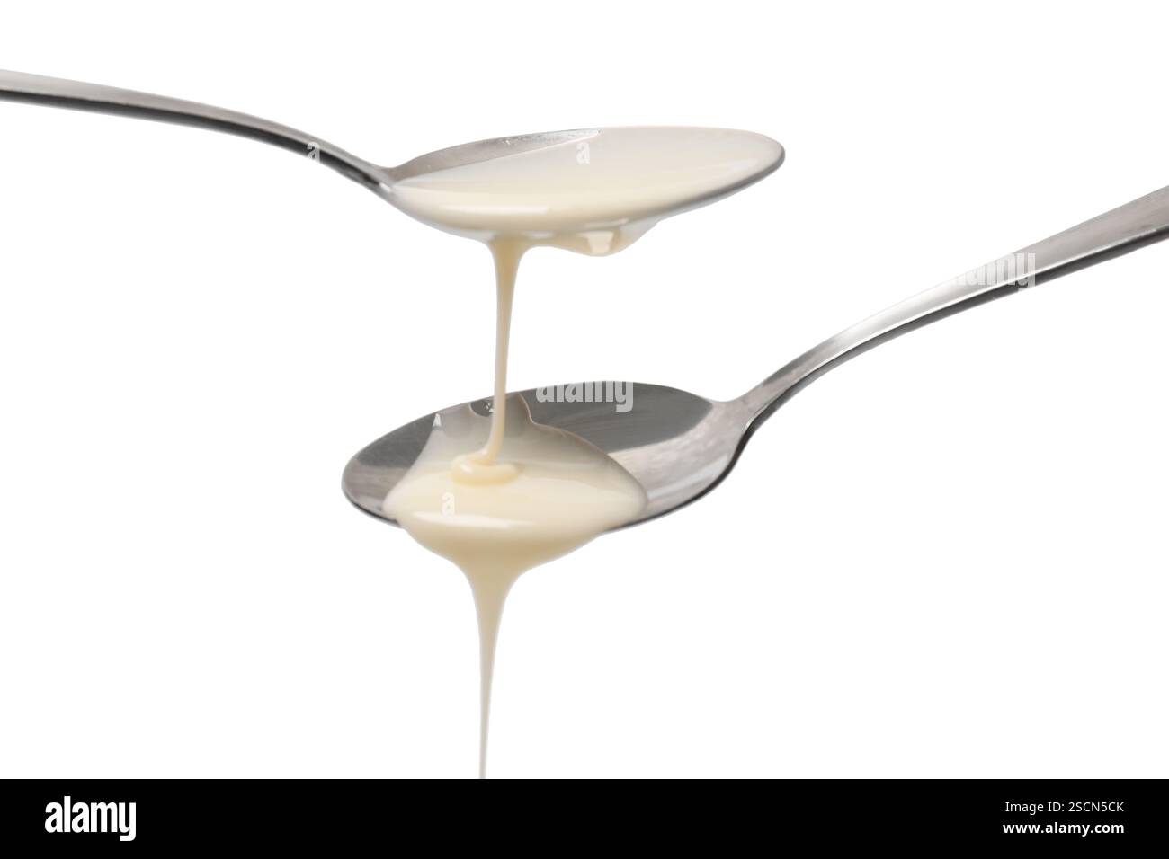 Condensed milk flowing down from spoons isolated on white Stock Photo ...