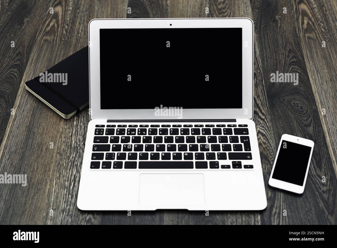 Computing setup with laptop, smartphone, and notebook on a wooden desk ...