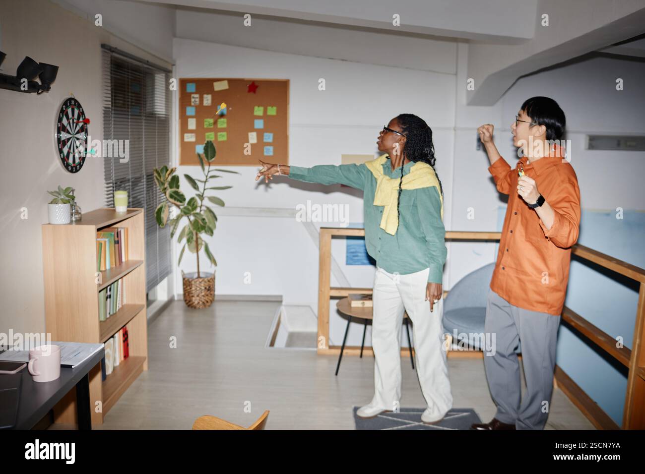 Colleagues enjoying a dart game during break in a modern office setting ...