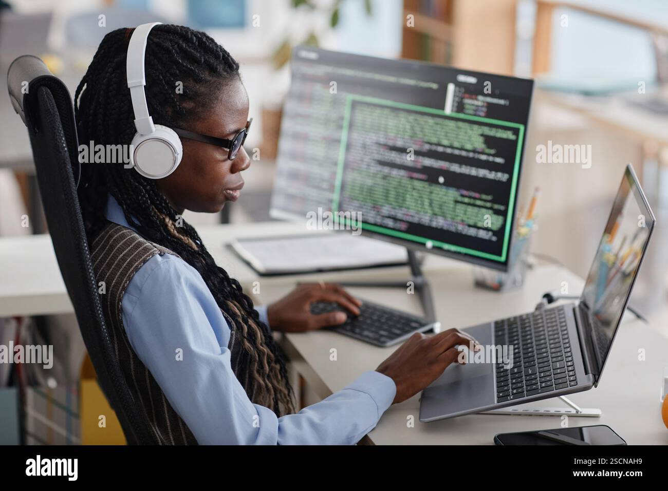 Female programmer deeply engaged in coding while wearing headphones and working with multiple ...