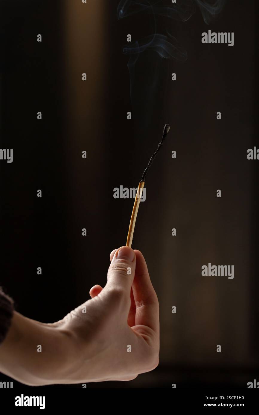 A hand holds an extinguished match on a dark background. The image has ...