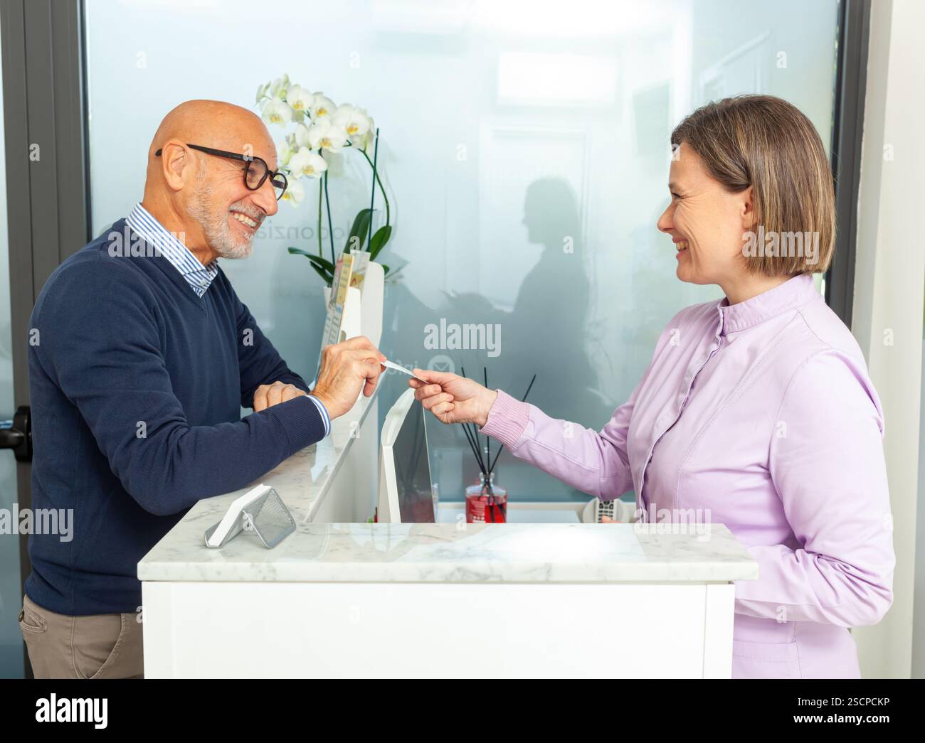 Senior man giving his health insurance card to the dentist secretary ...