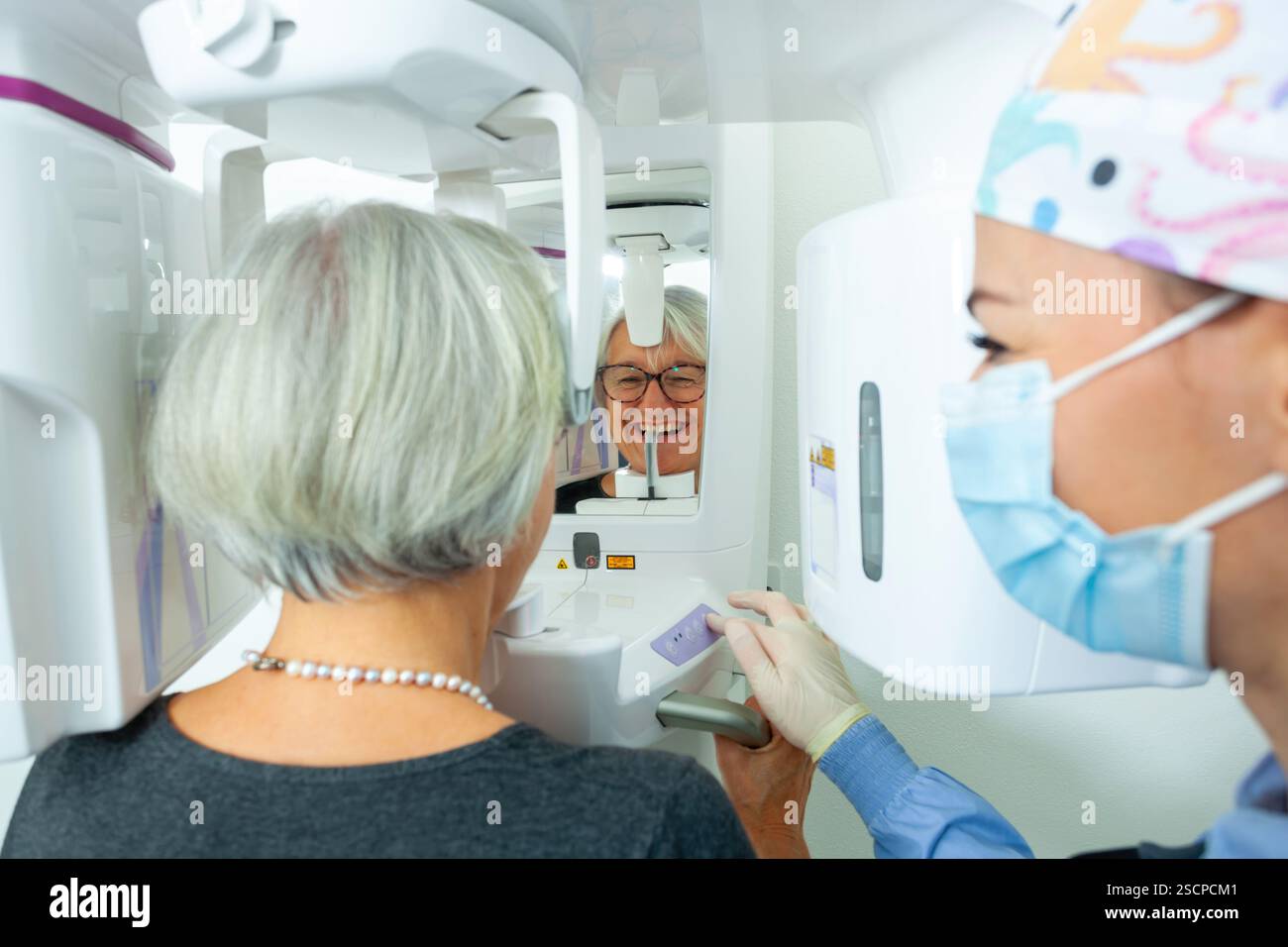 Dentist operating a dental x ray machine while examining a senior woman ...
