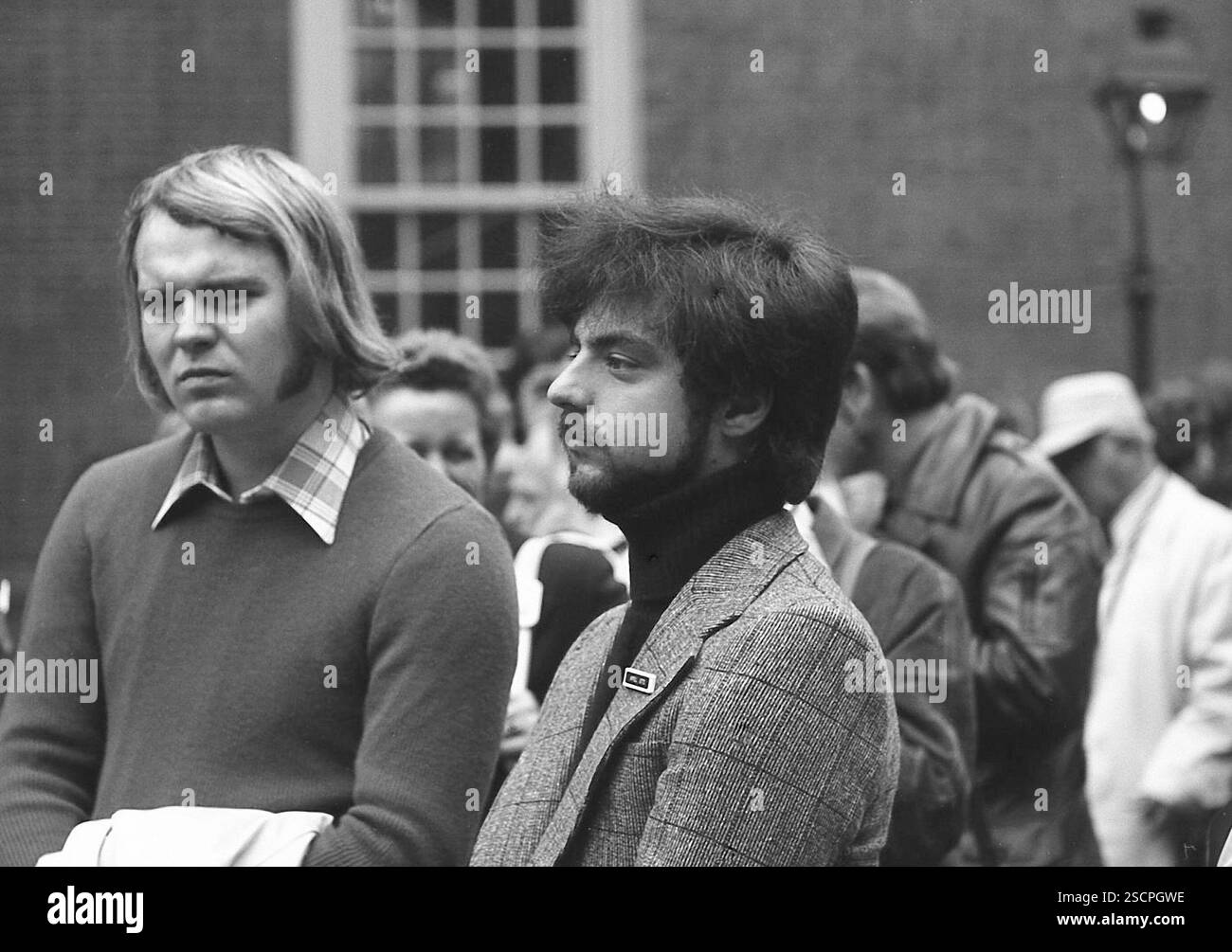 Two men in a crowd in New York City listen intently to a person talking ...