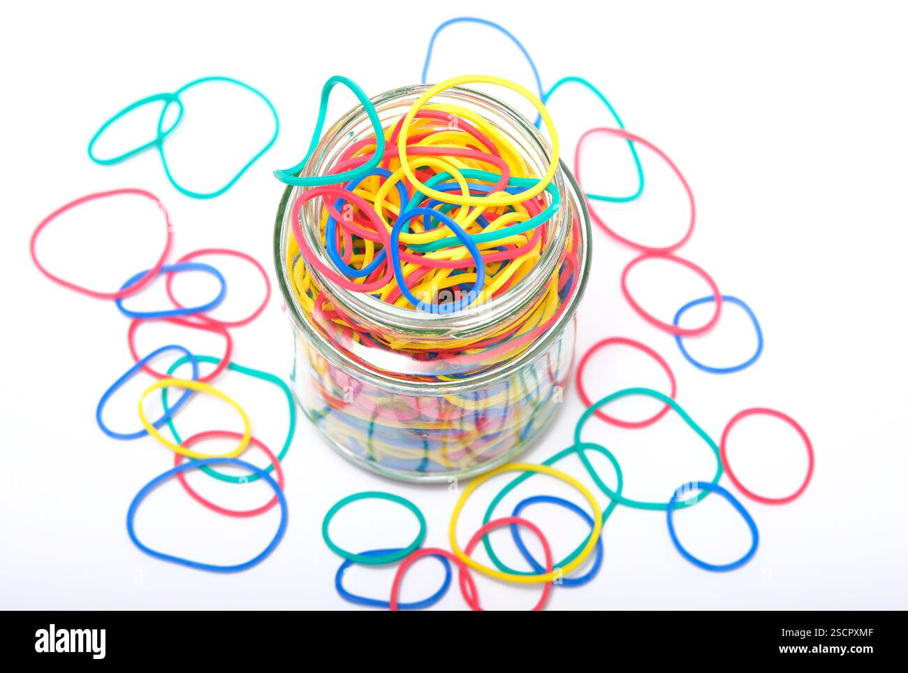 selection of colourful elastic bands in glass jar on white background ...
