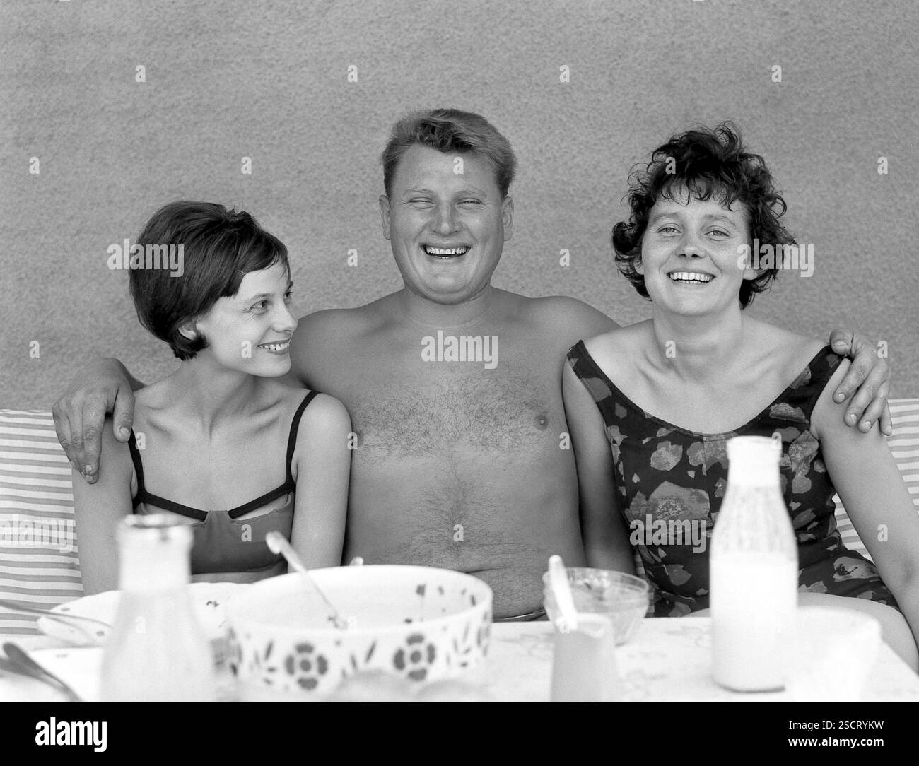 A man is sitting between two women with his arms around them ...
