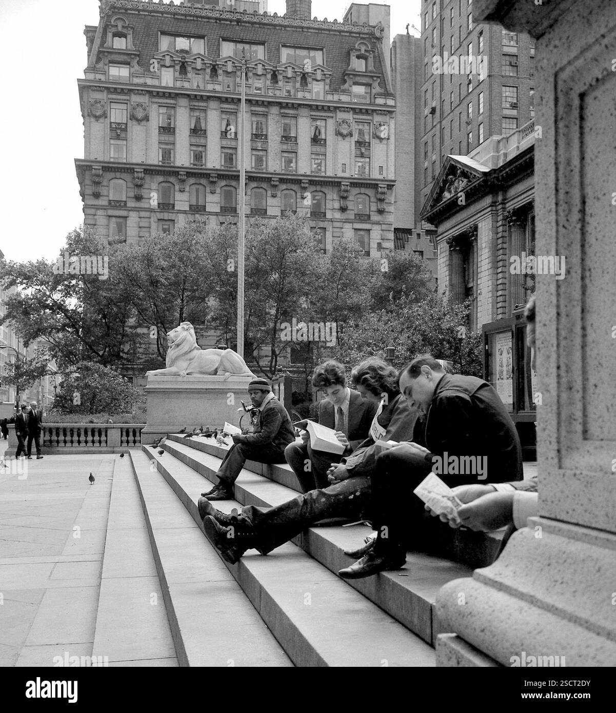Young people with books sit on the steps outside the New York Public ...