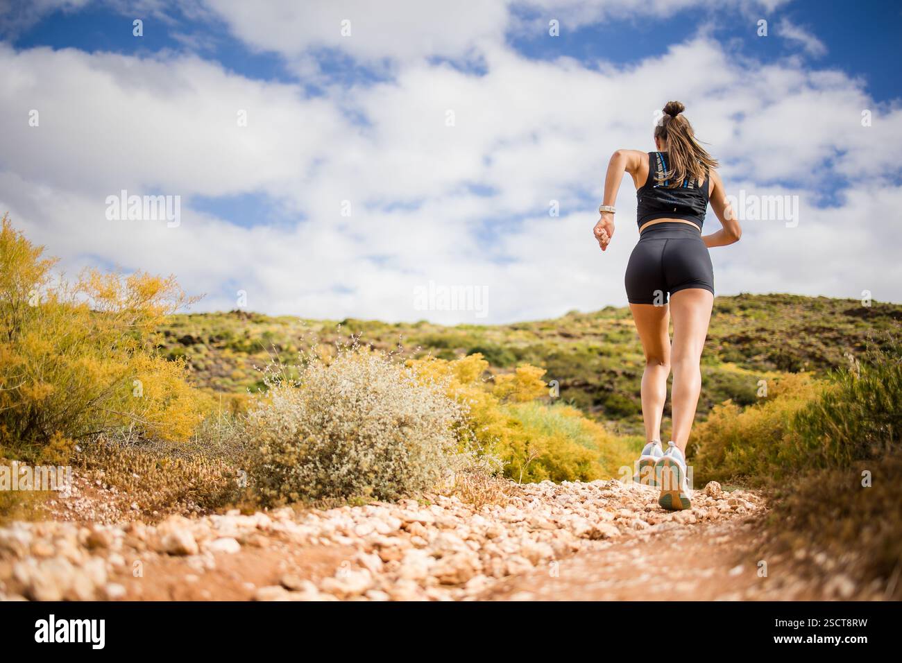 Female trail runner wearing black sportswear and a hydration vest, running through a scenic ...