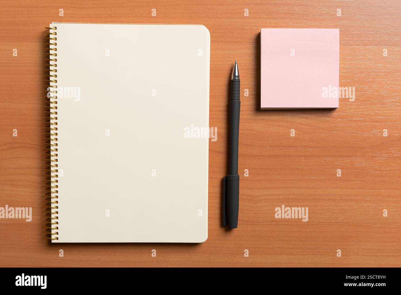 Blank notebook, pen, and sticky note arranged on a wooden desk in a ...