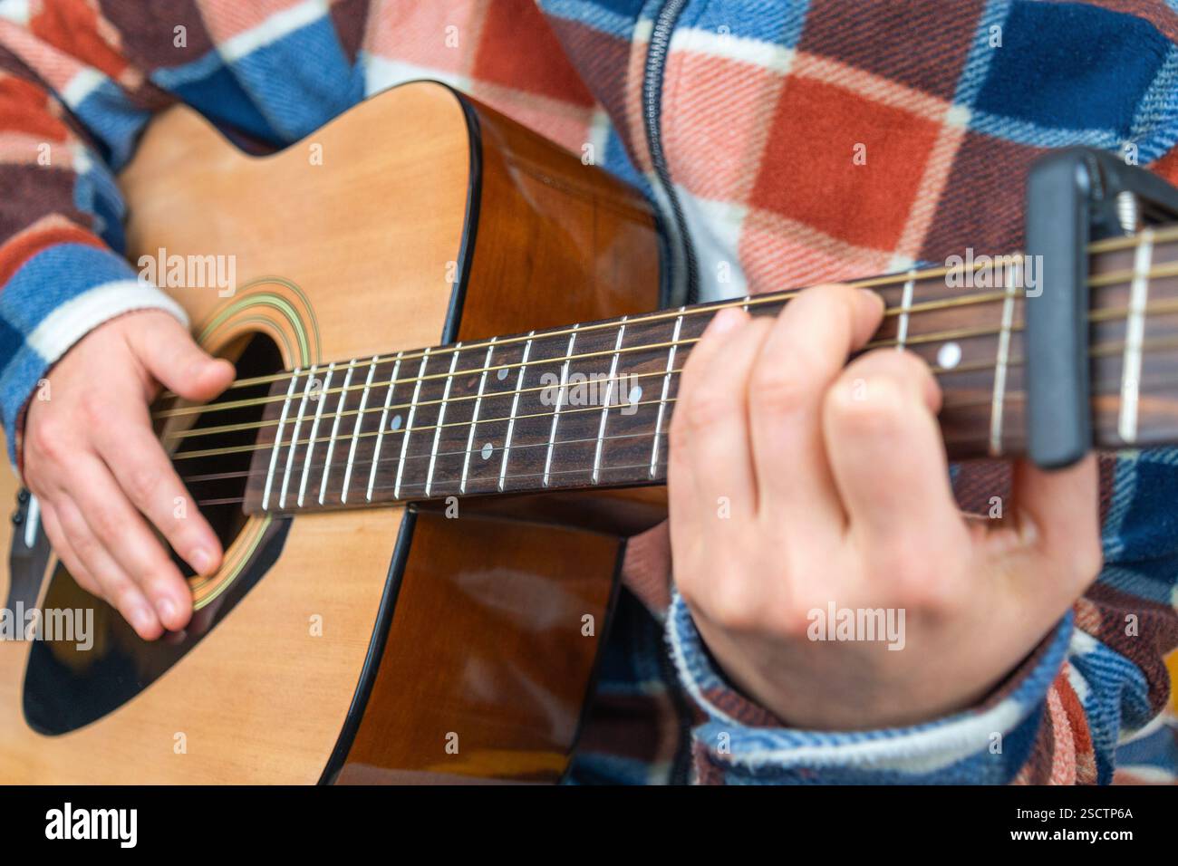 Person playing an acoustic guitar, wearing a plaid flannel. Left hand ...