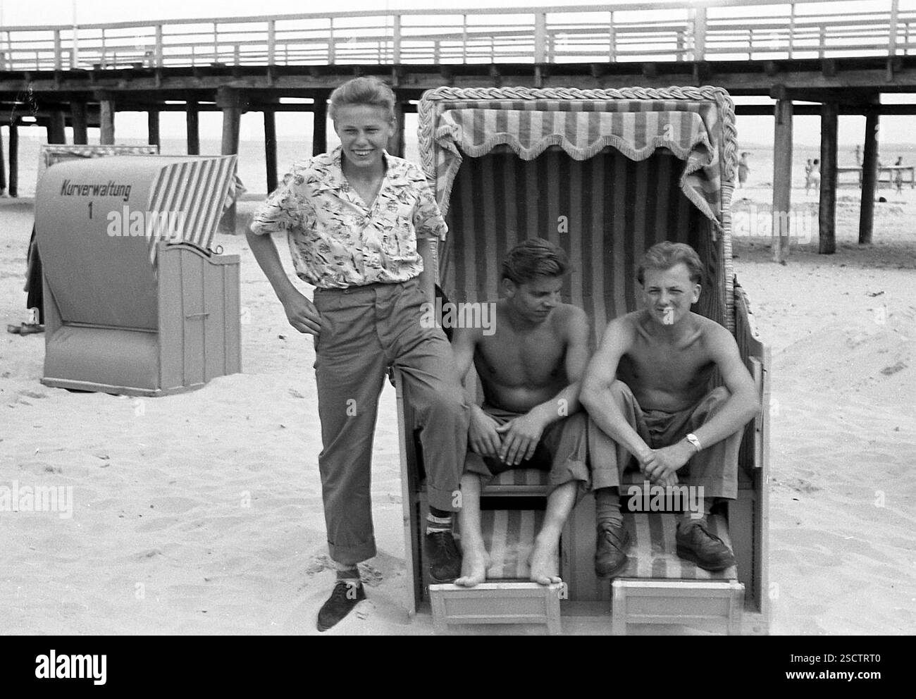 Three young men in a beach chair in front of the pier in Ahlbeck on the ...