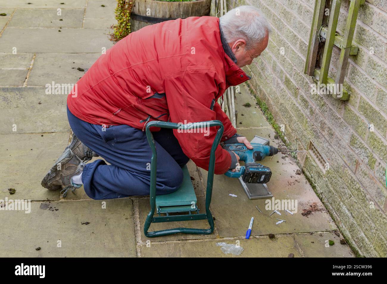 A male (man) using a cordless power drill to secure a cover over an air ...