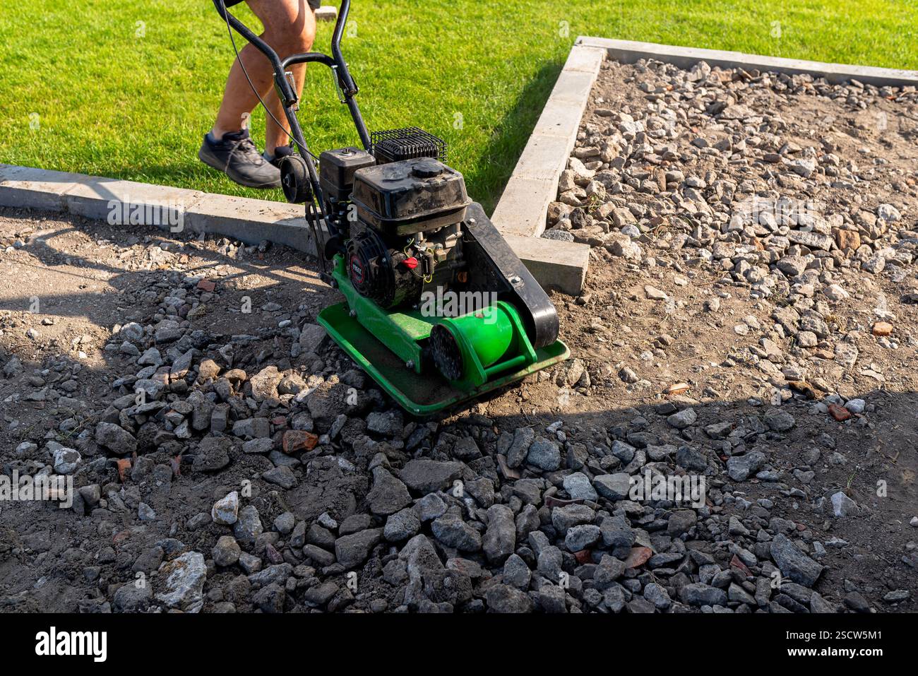 A man compacts rubble on a terrace under construction using a hand-held ...
