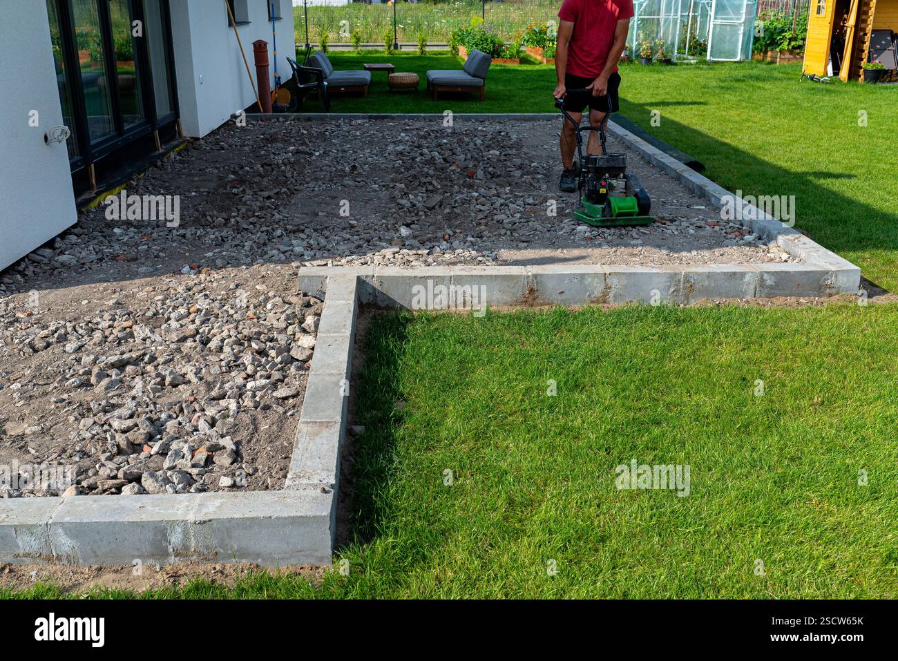 A man compacts rubble on a terrace under construction using a hand-held ...