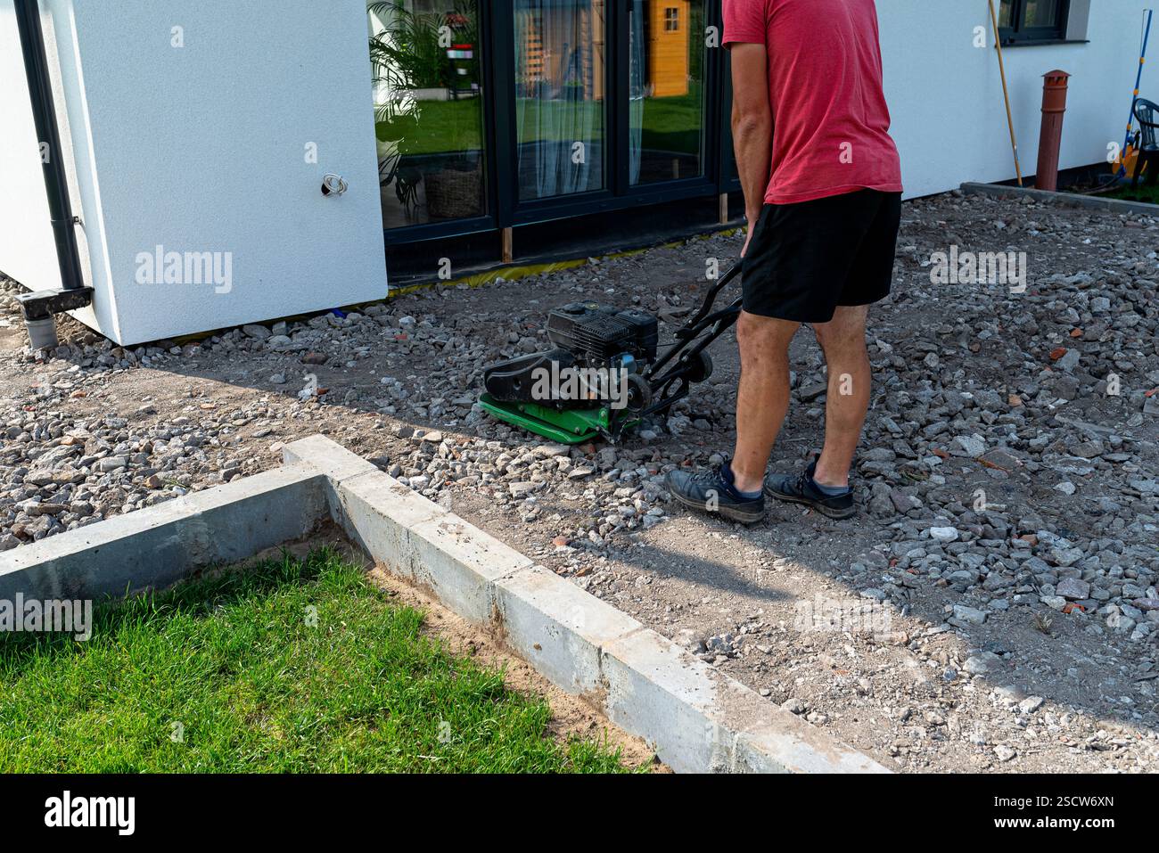 A man compacts rubble on a terrace under construction using a hand-held ...