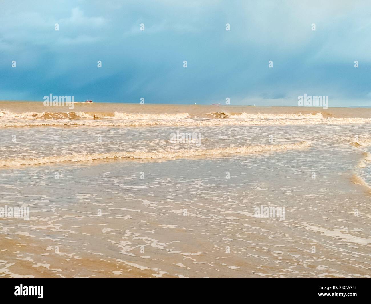 Gentle waves lap against the sandy beach as dark clouds hover overhead ...