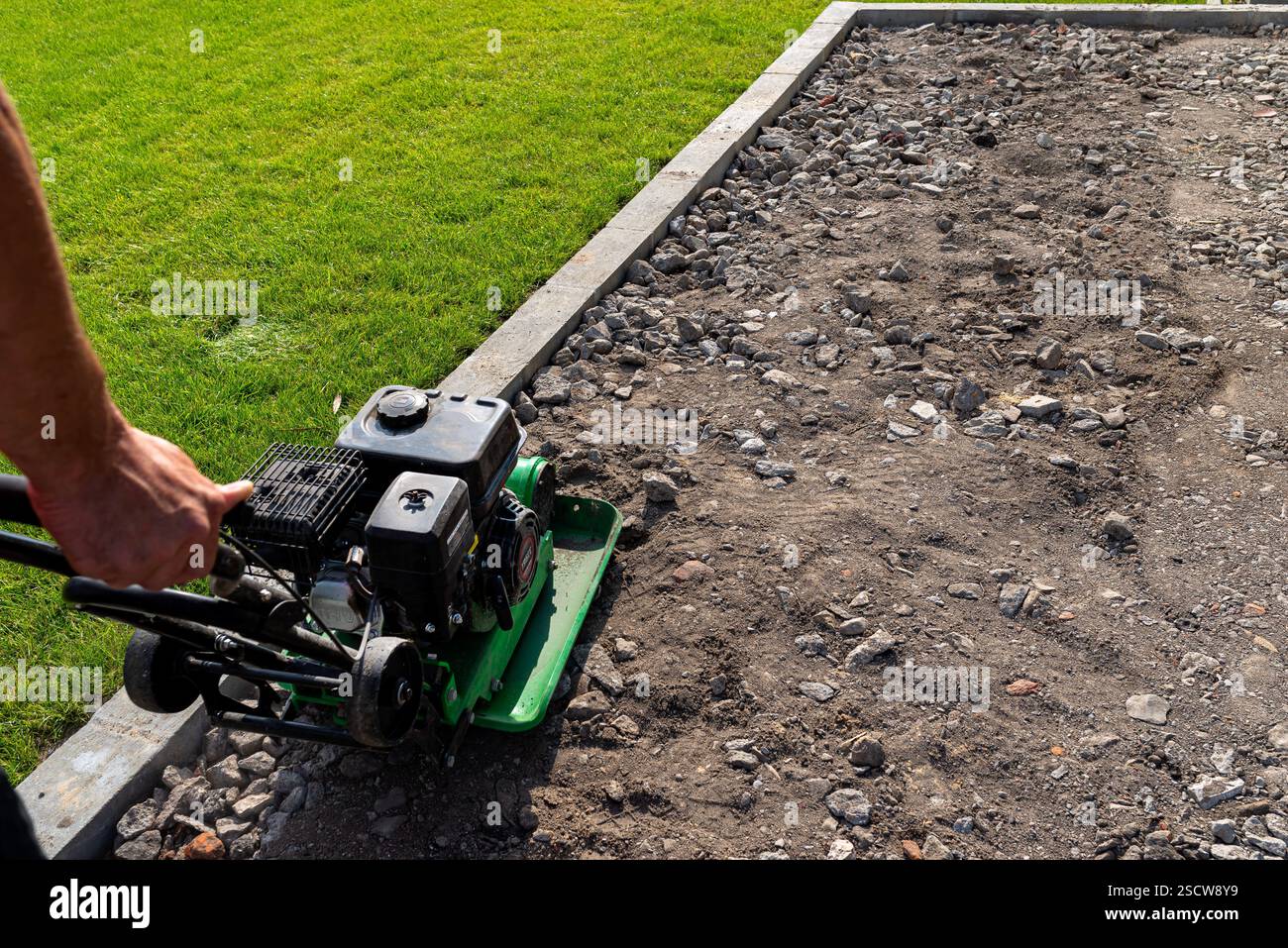 A man compacts rubble on a terrace under construction using a hand-held ...