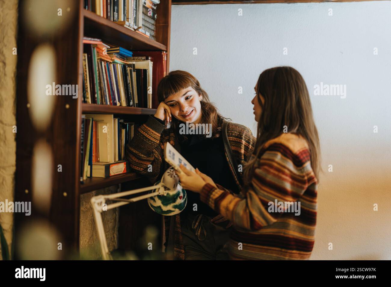 Two young women enjoying time in a cozy library filled with books and ...