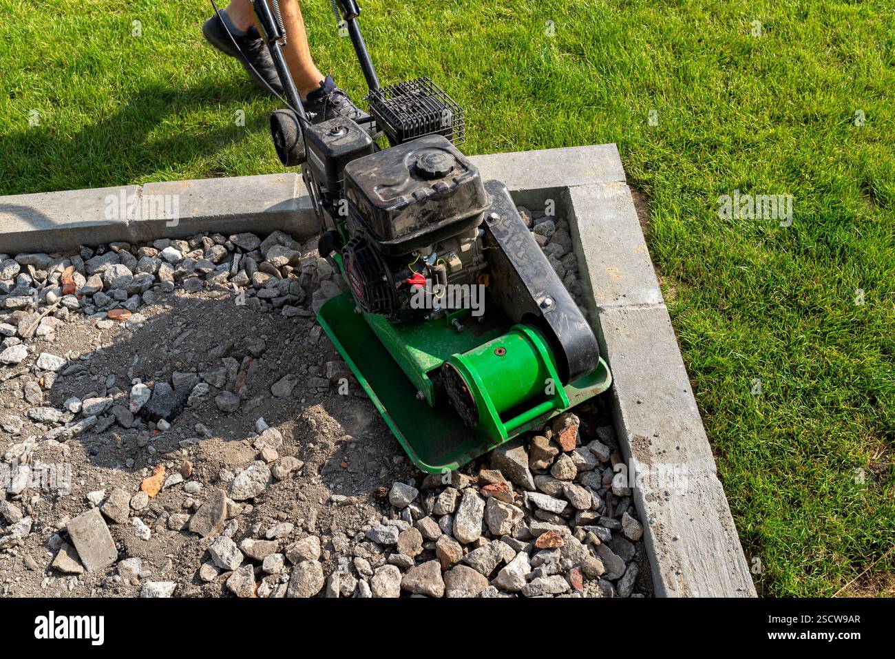 A man compacts rubble on a terrace under construction using a hand-held ...